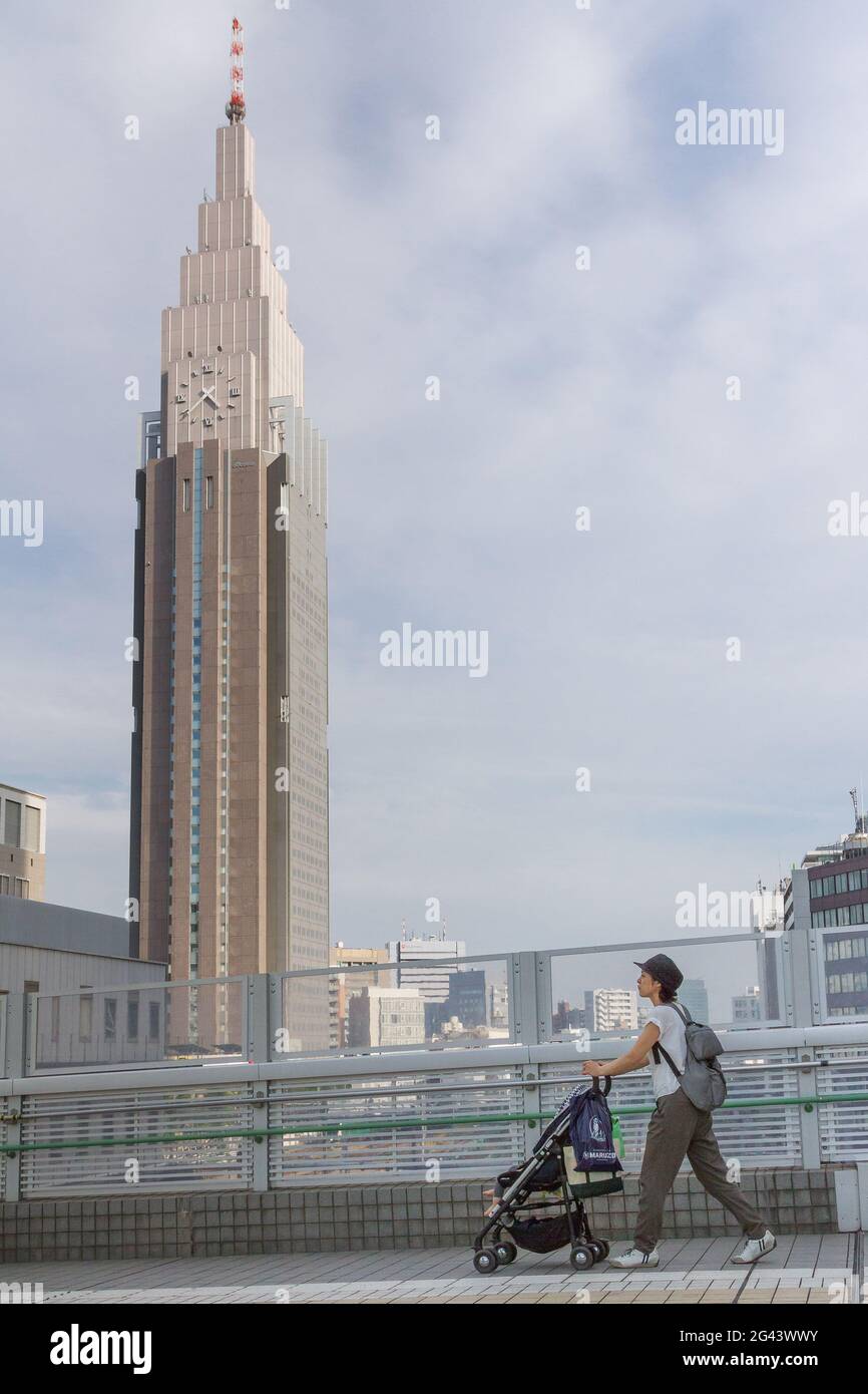 A mother wheels a pushchair in front of Docomo Tower in Shinjuku, Tokyo ...