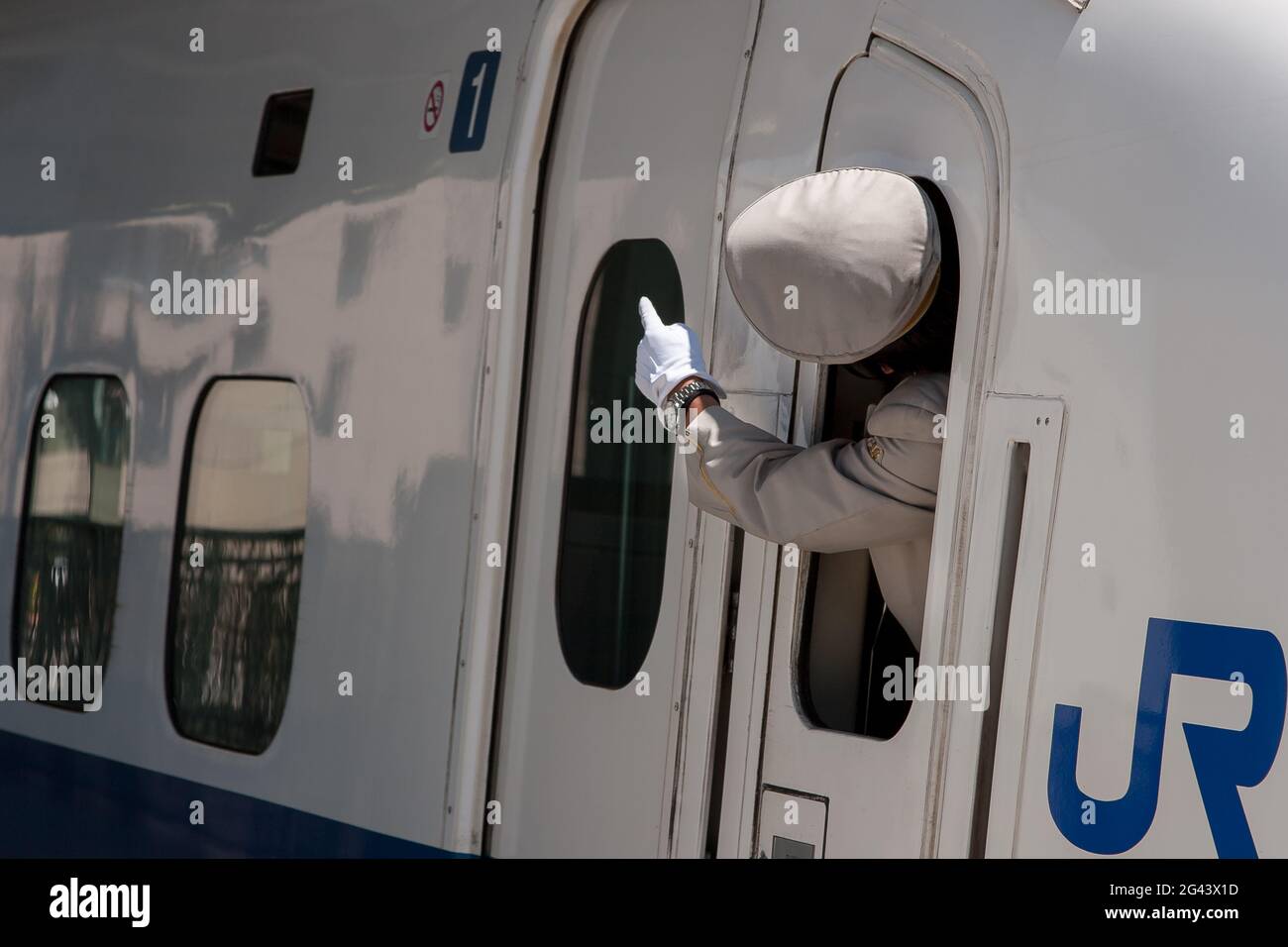 A guard points to a safety sign as he looks out of the window of a JR ...