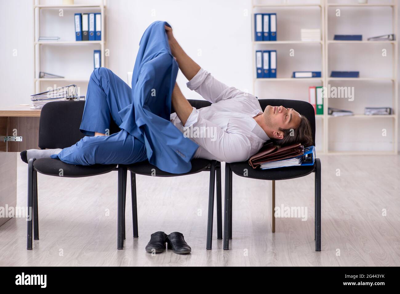 Young male employee sleeping in the office on chairs Stock Photo - Alamy