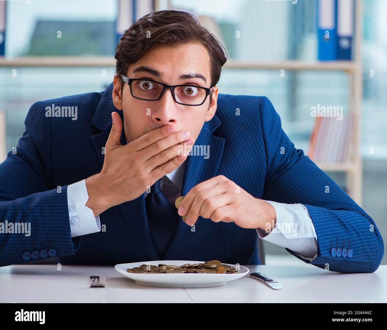 Funny businessman eating gold coins in office Stock Photo - Alamy