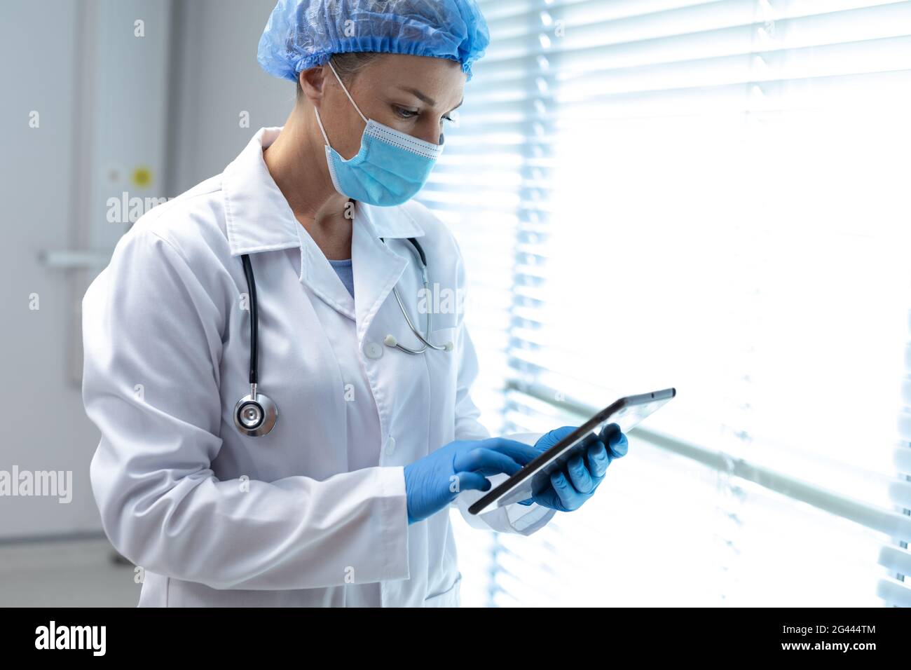 Caucasian female doctor wearing mask and latex gloves using tablet ...