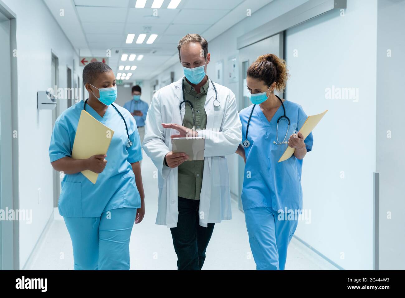 Diverse group of male and female doctors wearing face masks walking ...