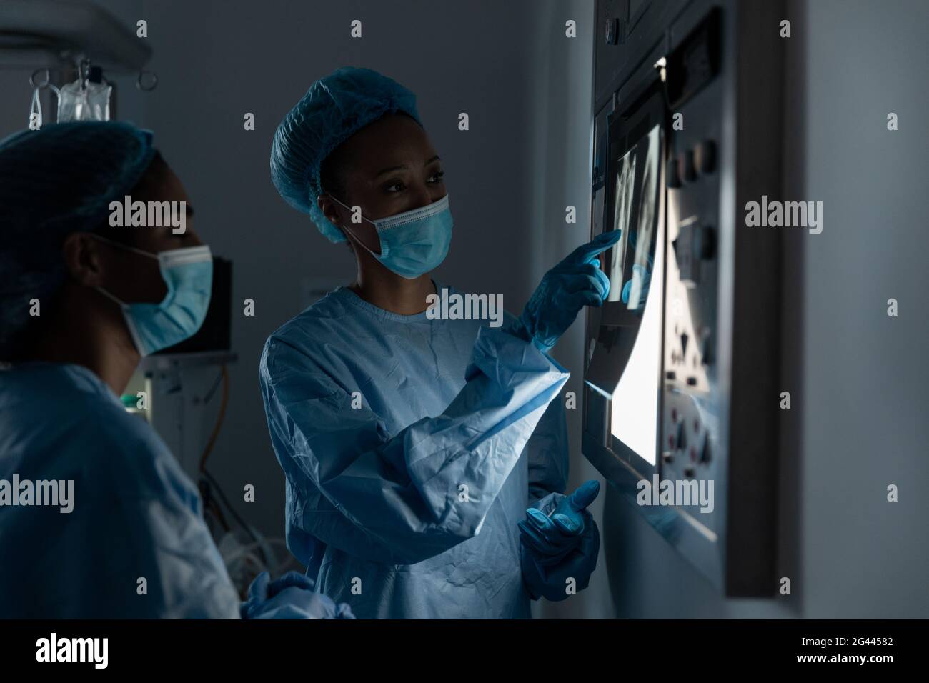 Diverse female doctors wearing face masks and surgical overalls looking ...