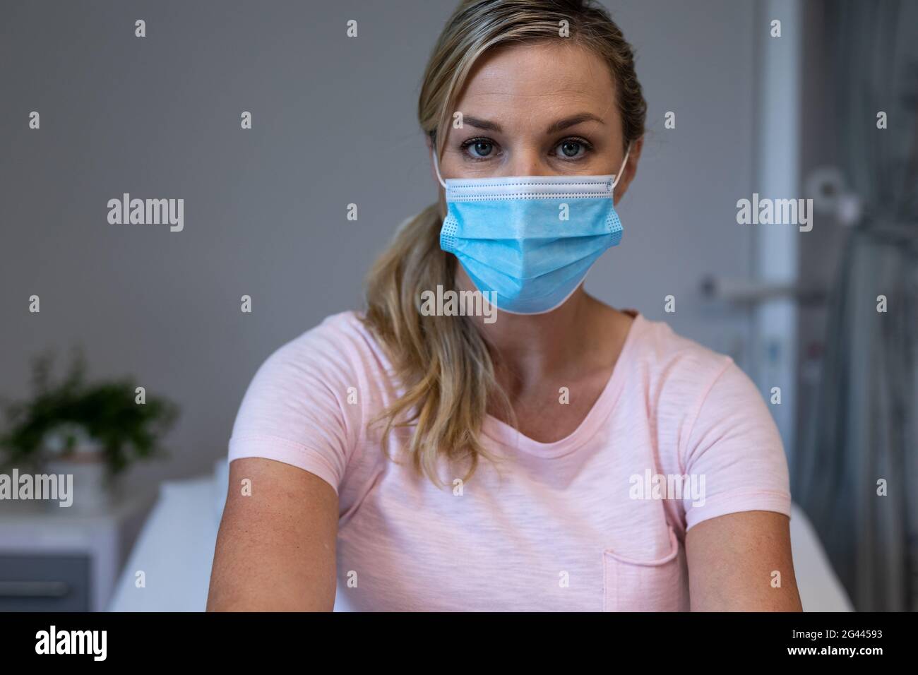 Portrait of caucasian female patient wearing mask sitting on hospital ...