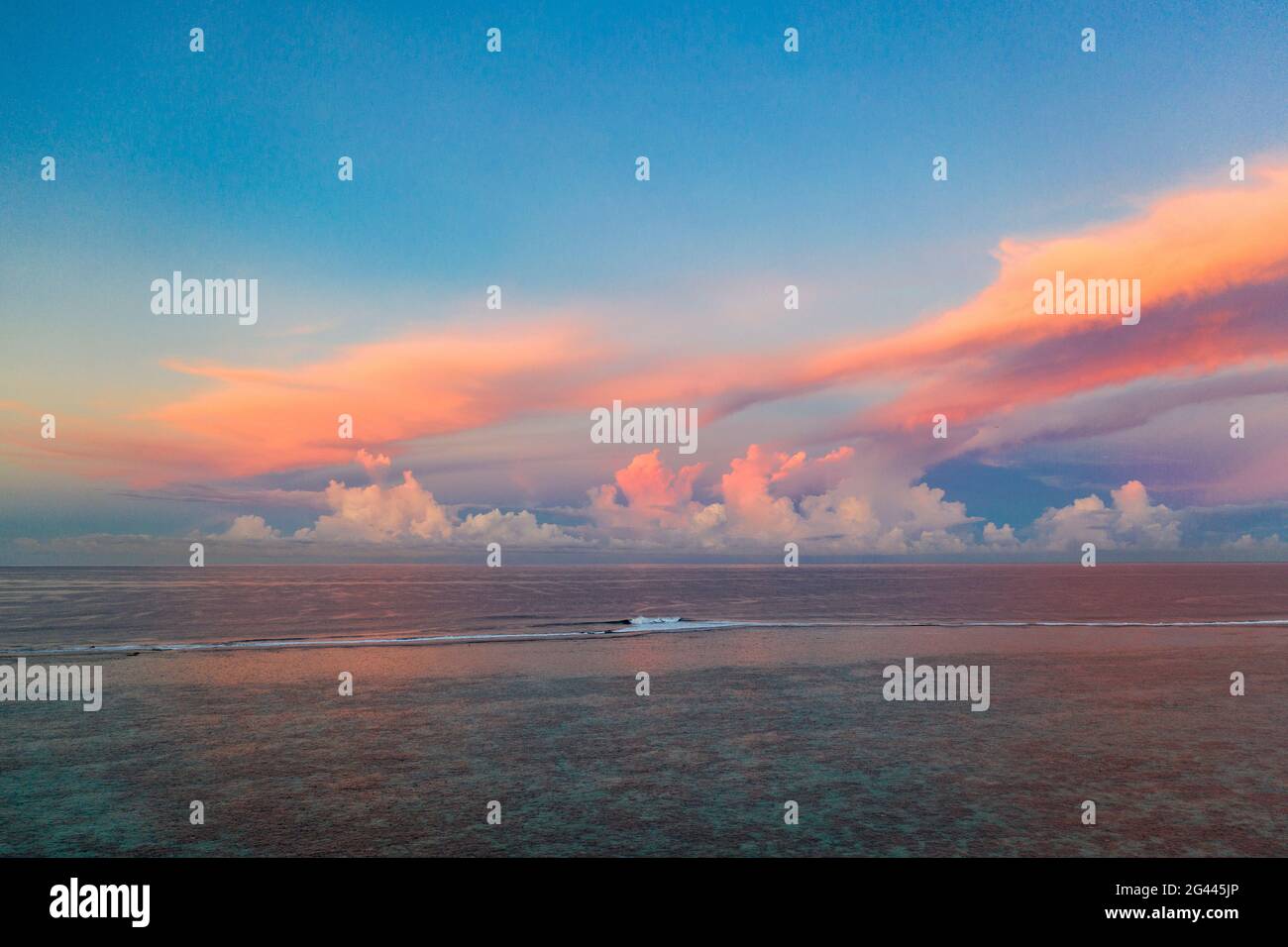 Aerial view of waves breaking on the reef with sunset clouds behind ...