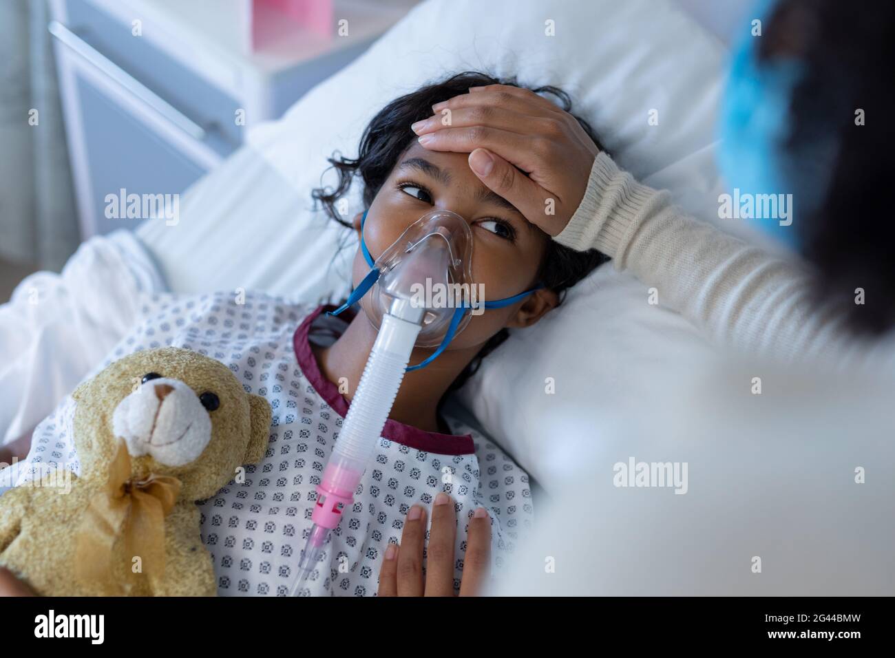 Mixed race mother in face mask touching sick daughter's forehead on ...