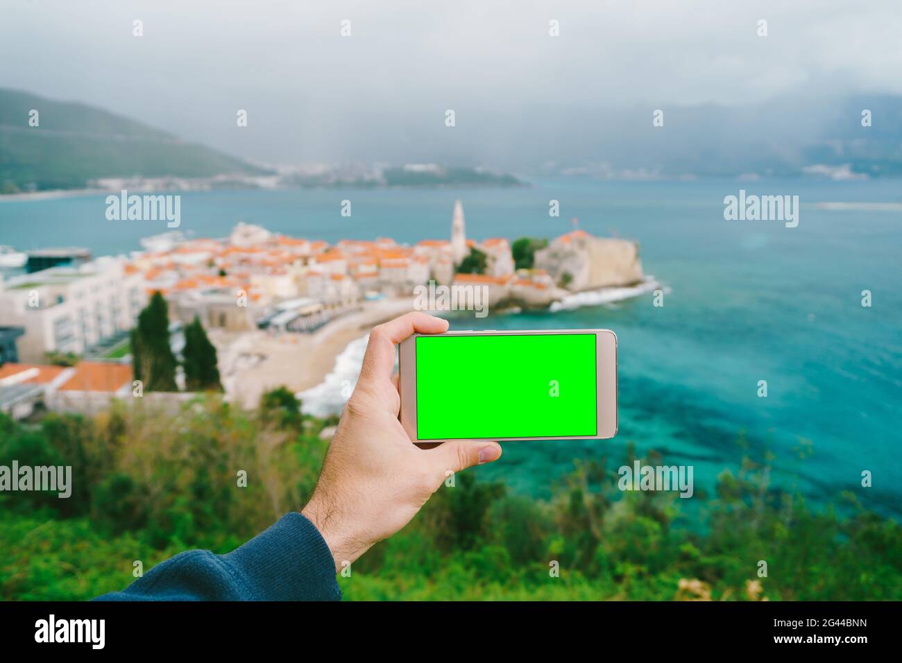 Hand holds a phone with a blank screen. The old town can be seen in the ...