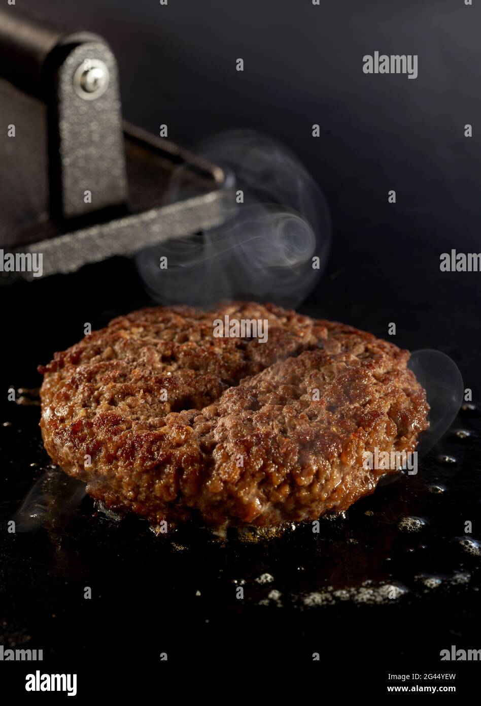 Thick juicy beef patty sizzling on the grill with waftng steam in a ...