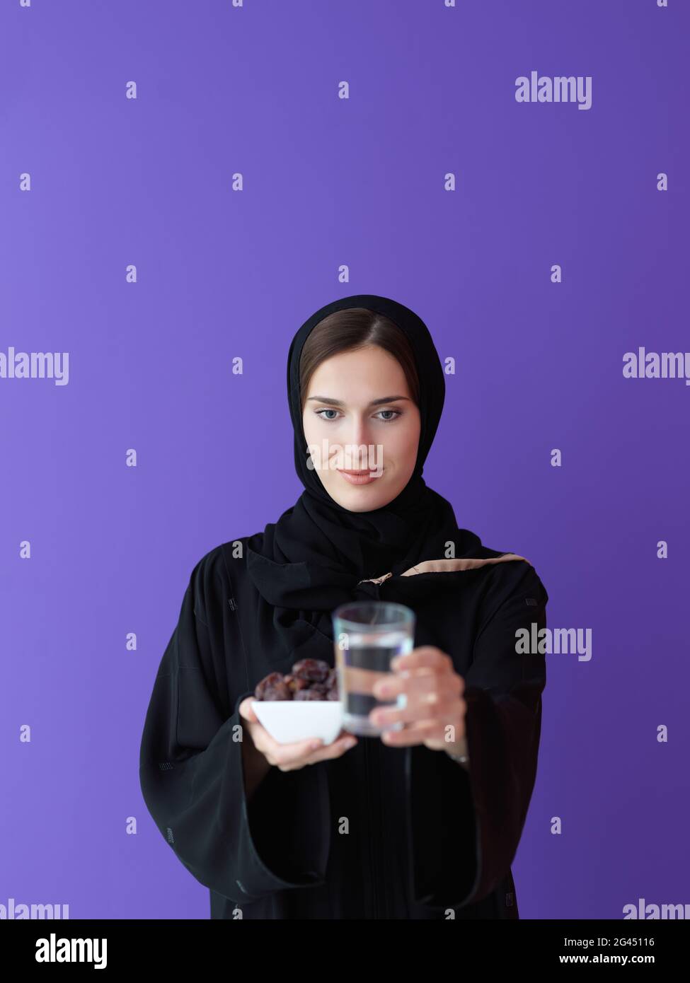 Modern muslim woman in abaya holding a date fruit and glass of water in ...