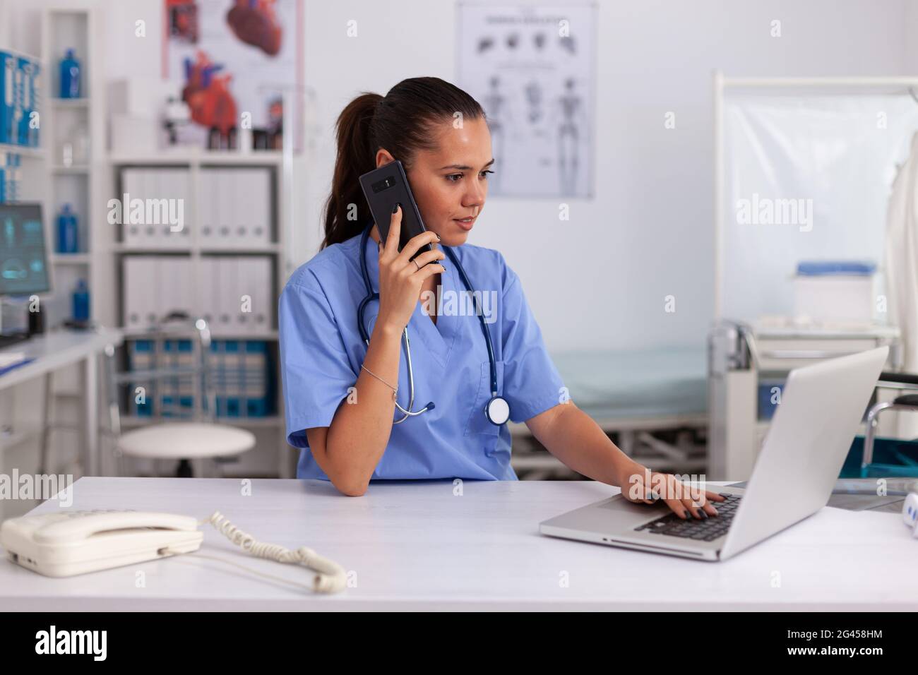 Medical practitioner using telephone and laptop in hospital office ...