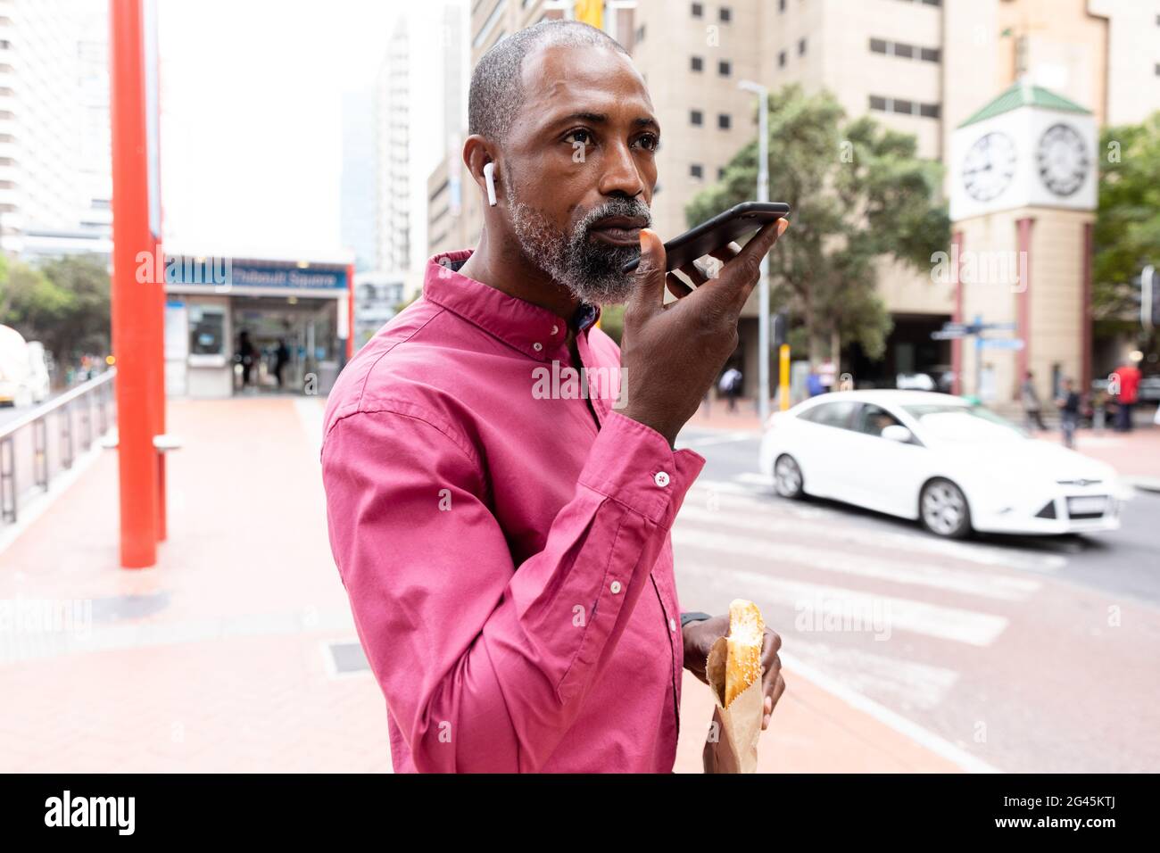 African American man using his phone and eating a takeaway sandwich ...