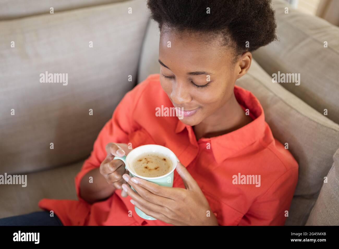 Woman holding coffee cup while sitting on the couch Stock Photo - Alamy