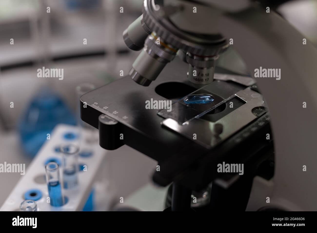 Part of microscope and flasks with blue liquid substance in chemical ...