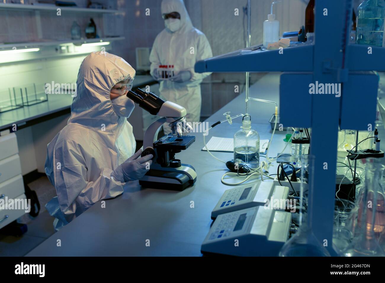 Scientist using microscope while her colleague carrying flasks with ...