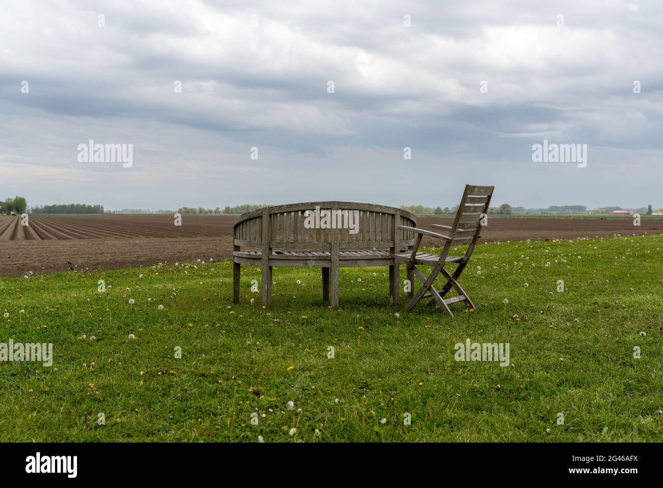 Empty wooden garden furniture on a green field under an overcast sky ...
