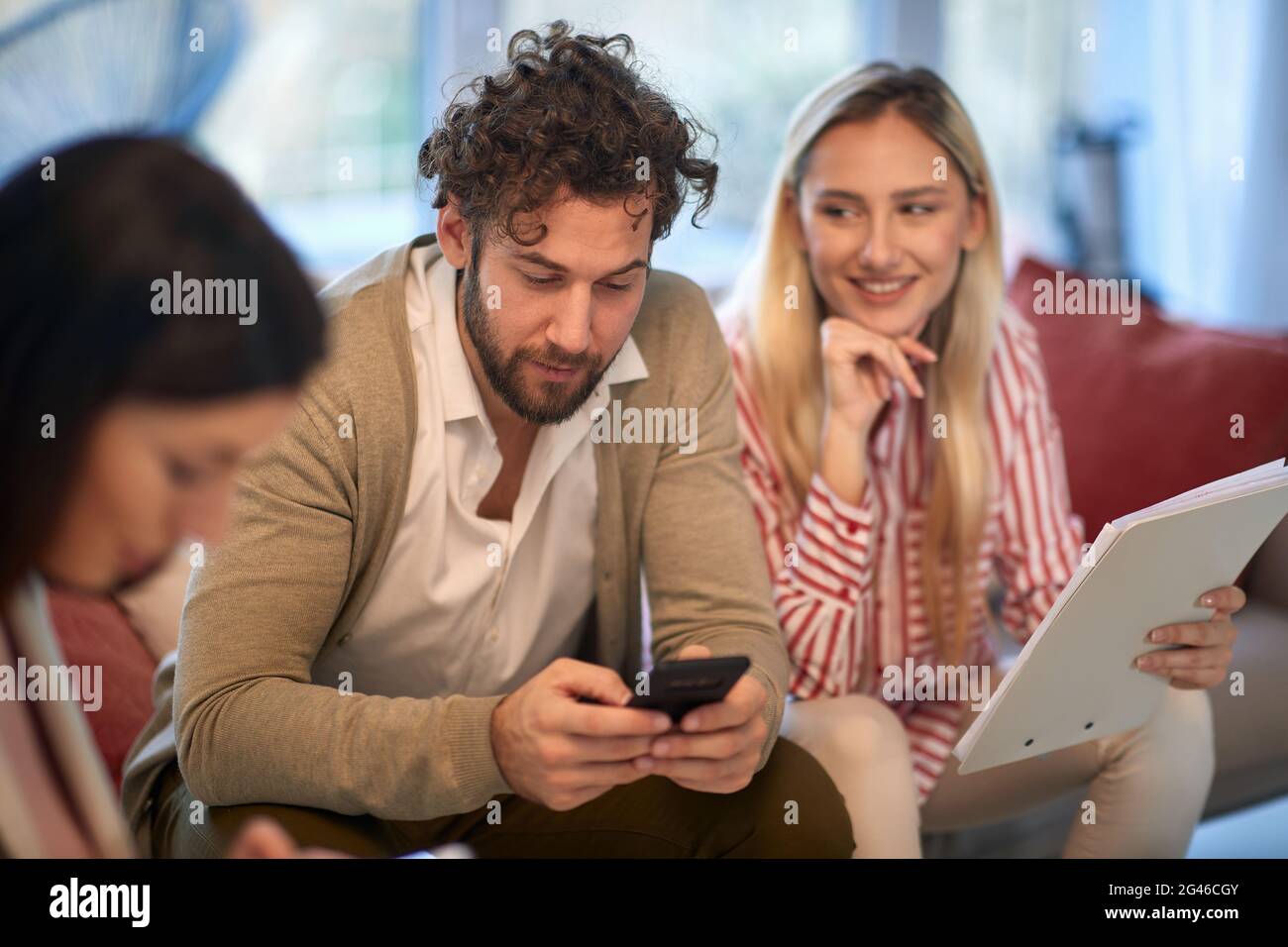 A young businessman texting on a smartphone at a meeting in a relaxed ...
