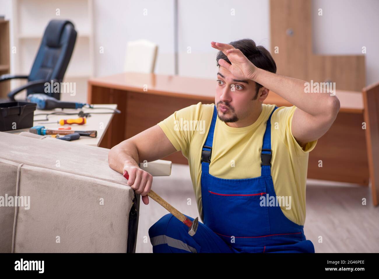 Young carpenter repairing arm-chair in the office Stock Photo - Alamy