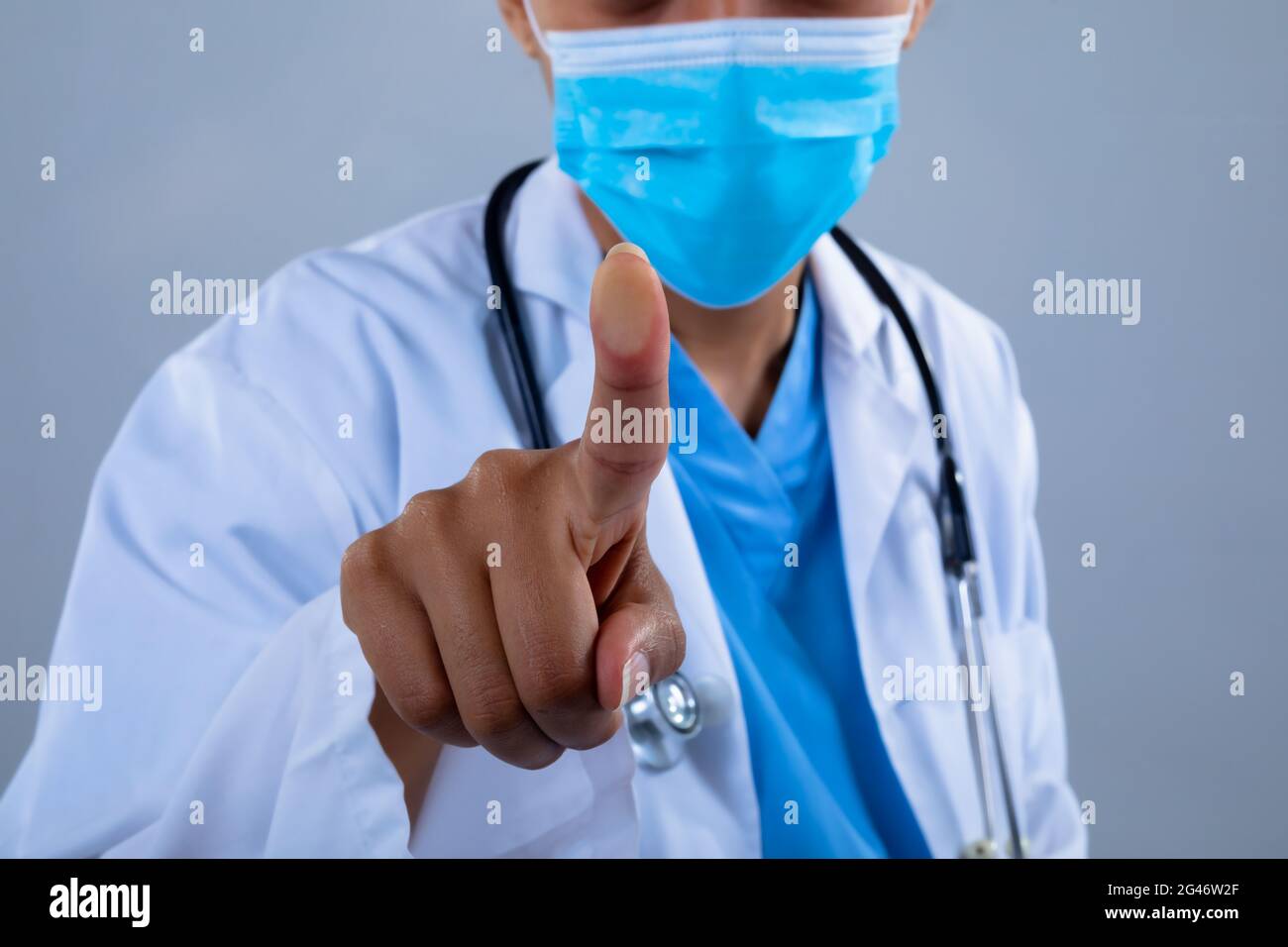 Mid section of doctor wearing face mask touching invisible screen ...