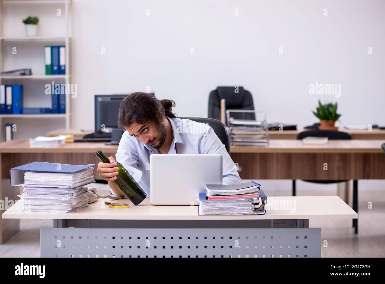 Young male employee drinking alcohol at workplace Stock Photo - Alamy