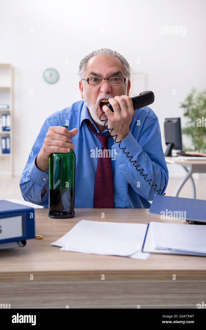 Senior male employee drinking alcohol in the office Stock Photo - Alamy