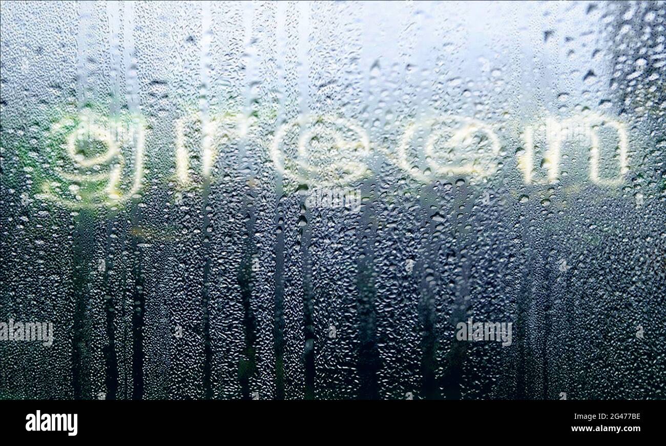 GREEN text neon sign as seen through a glass window with dripping rain ...