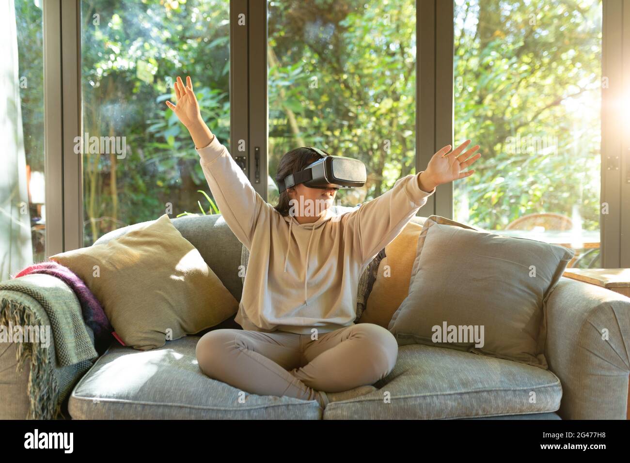 Smiling asian girl wearing vr headset with arms outstretched sitting on ...