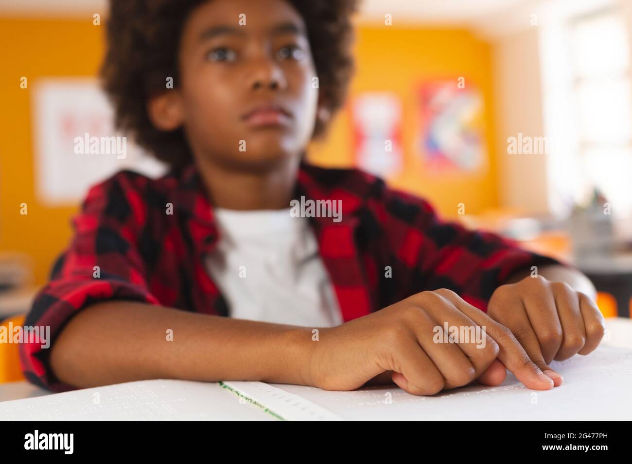 Blind african american schoolboy sitting at desk in classroom reading ...