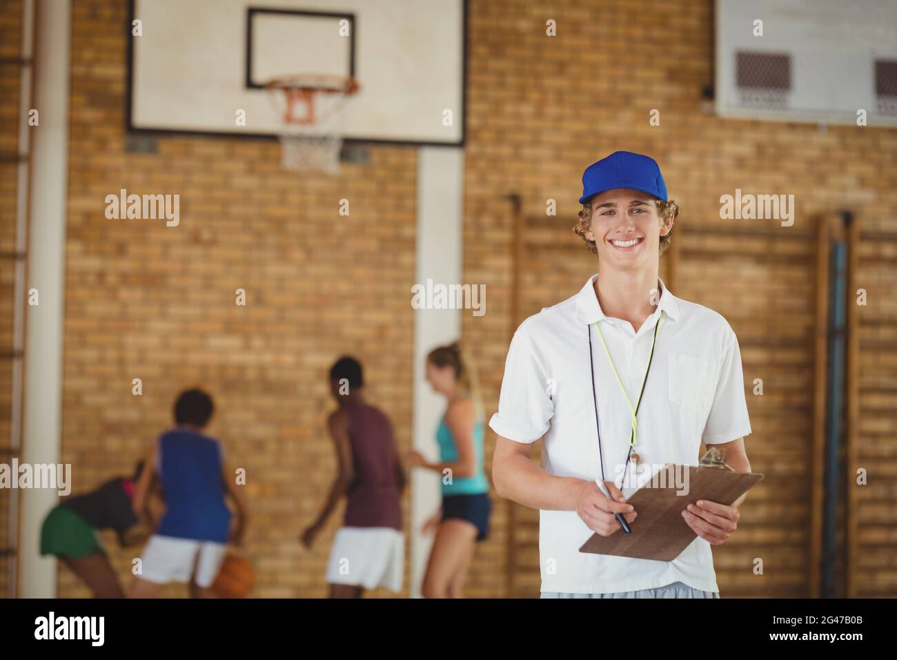 Coach smiling at camera while high school team playing basketball in ...