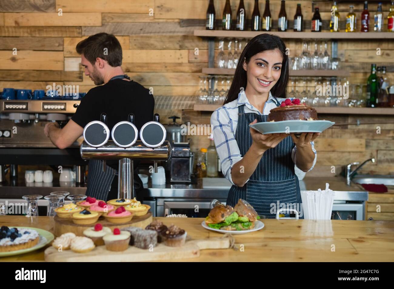Portrait of smiling waitress holding a chocolate cake at counter Stock ...