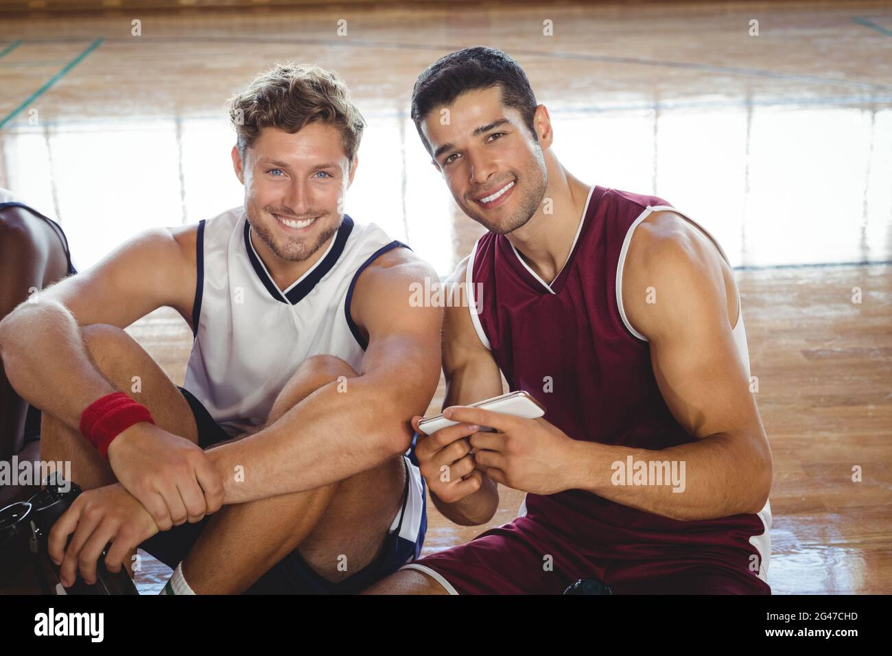 Portrait of smiling basketball players using mobile while relaxing ...