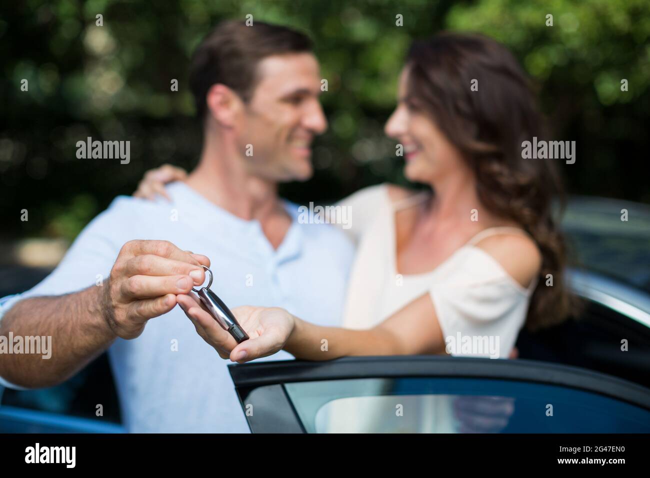 Man giving key to woman by car Stock Photo - Alamy