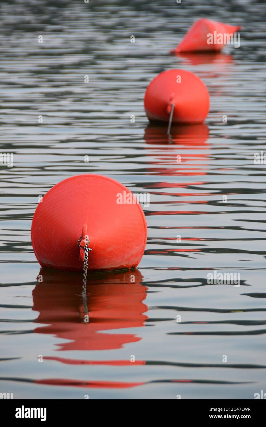 Vertical shot of three red buoys floating on the surface of a river ...