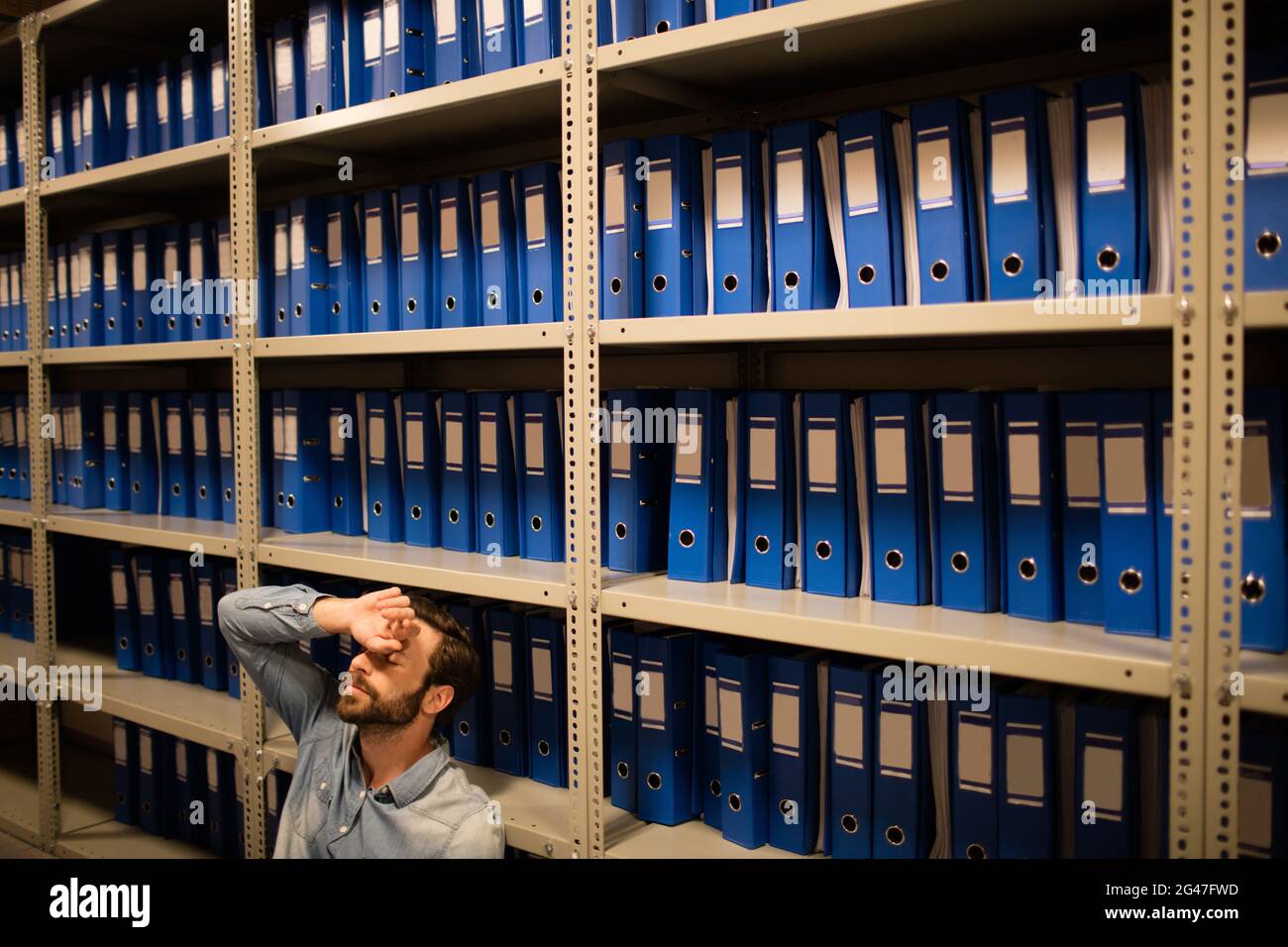Tired businessman sitting in file storage room Stock Photo - Alamy