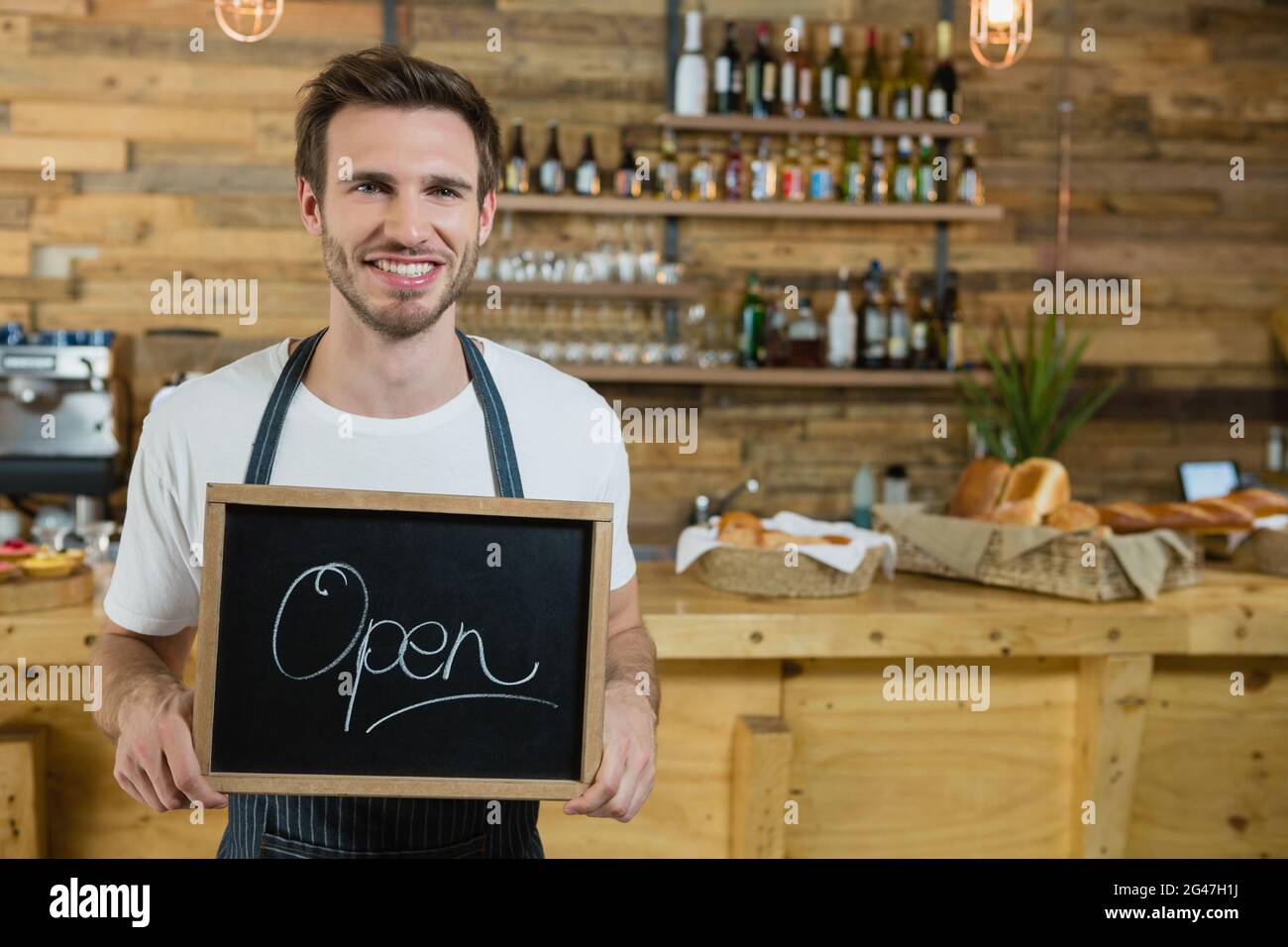 Portrait of smiling waiter standing with open signboard at counter ...