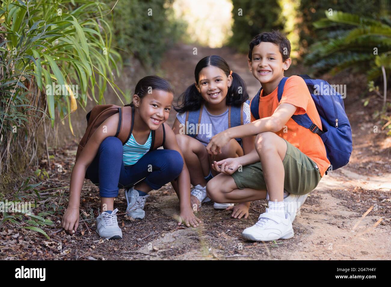 Smiling friends crouching on field at natural parkland Stock Photo - Alamy