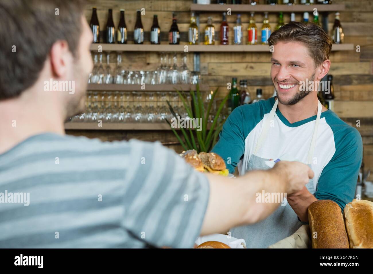 Smiling waiter serving to customer at counter Stock Photo - Alamy