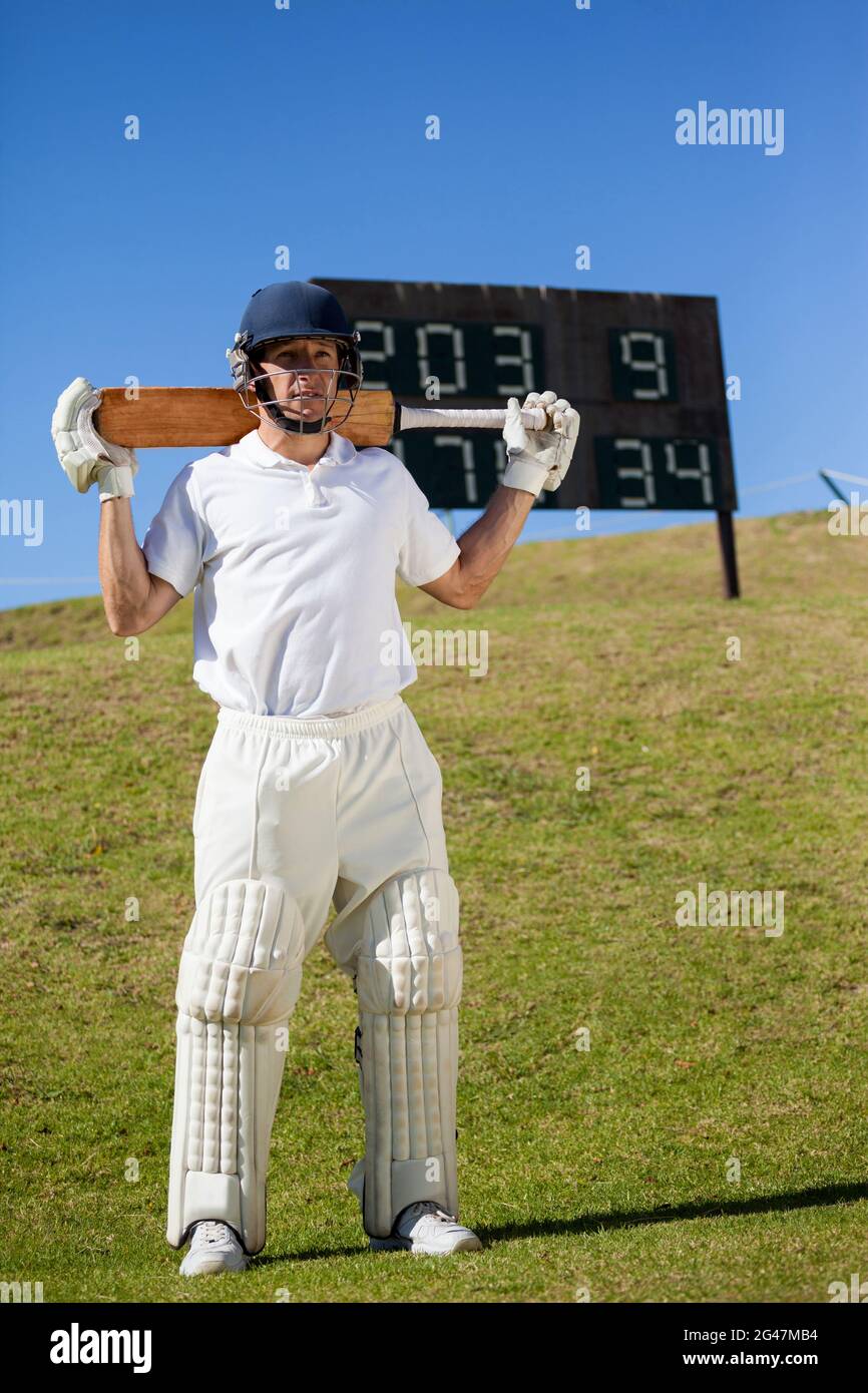 Cricket player holding bat while standing on field Stock Photo - Alamy