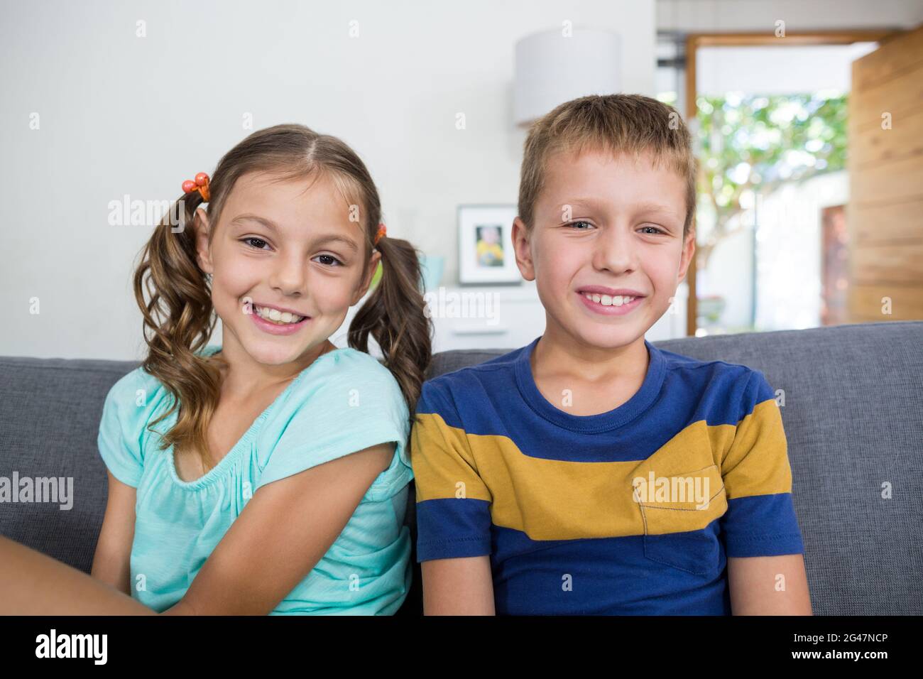 Smiling siblings sitting together on sofa in living room Stock Photo ...