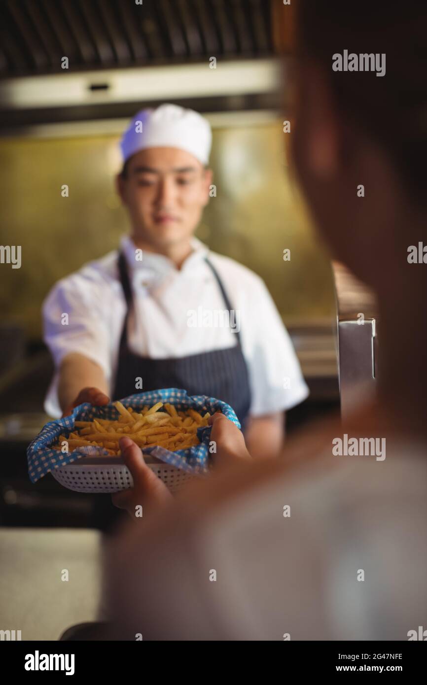 Chef passing tray with french fries to waitress Stock Photo - Alamy