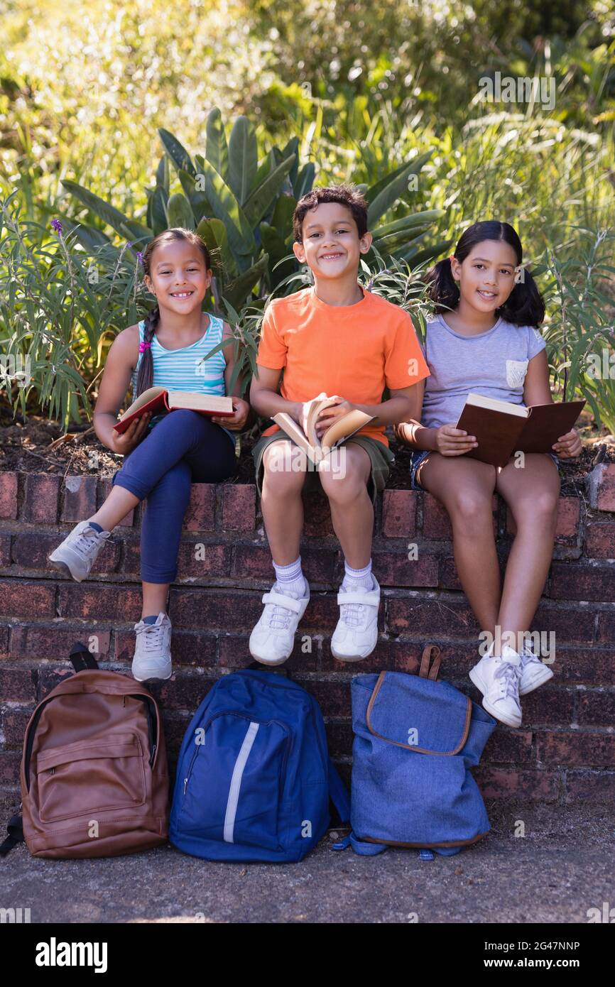 Smiling friends holding books while sitting on retaining wall Stock ...