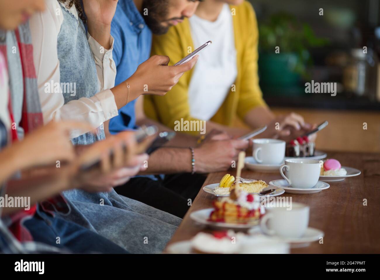 Group of friends using mobile phone while sitting at table Stock Photo ...