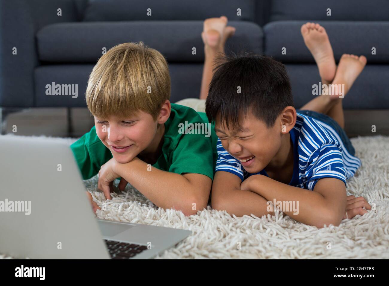 Smiling siblings lying on rug and using laptop in living room Stock ...