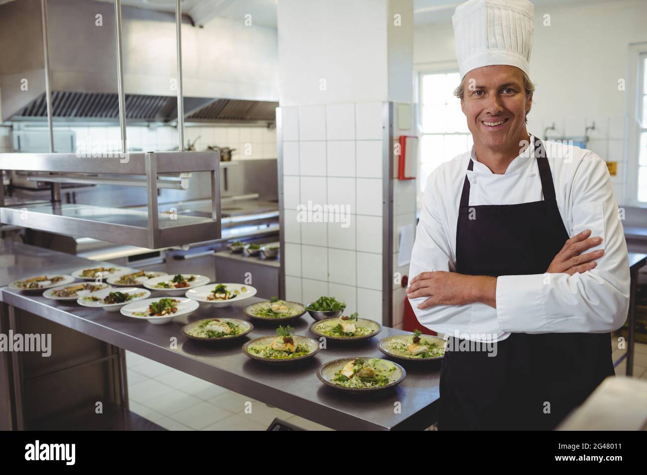 Portrait of happy chef with standing with arms crossed at order station ...