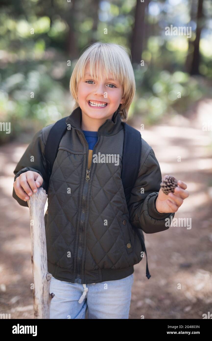 Smiling little boy holding pine cone while standing in forest Stock ...