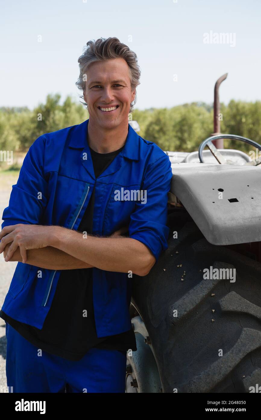 Worker leaning with arms crossed near tractor Stock Photo - Alamy