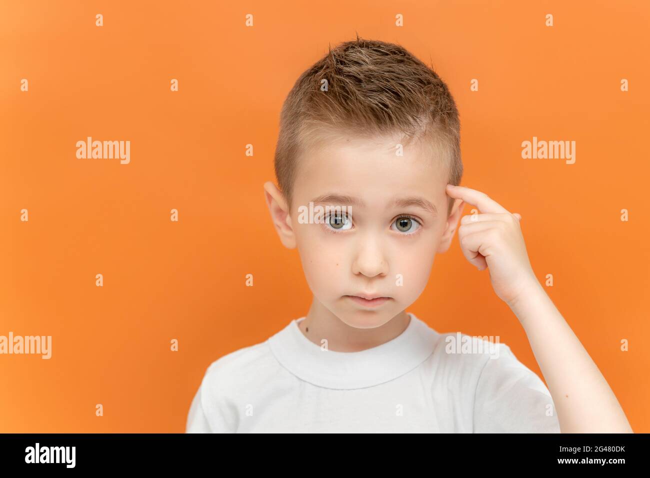 Little boy points a finger to his head isolated on an orange background ...