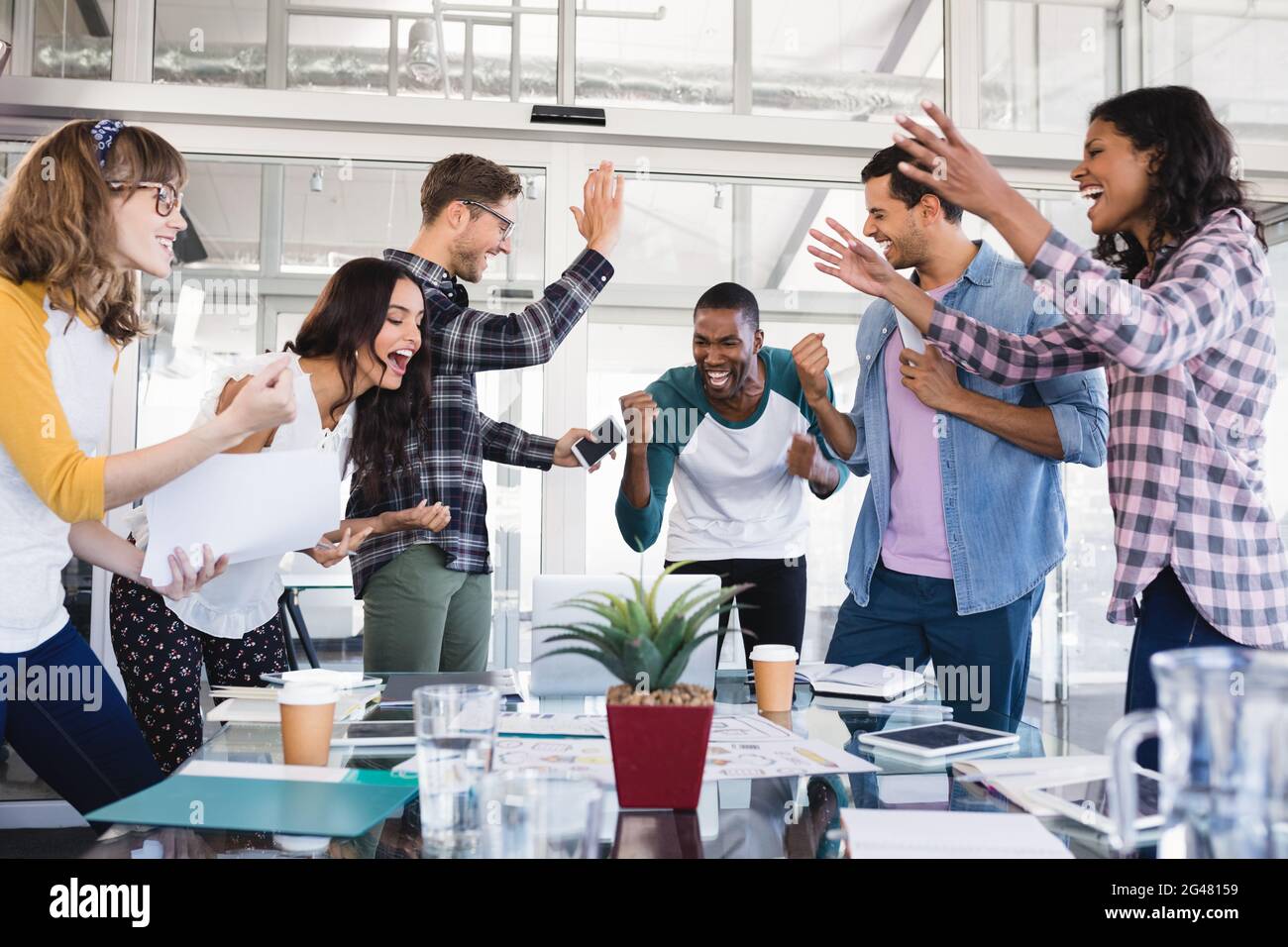 Cheerful creative business team standing around table Stock Photo - Alamy