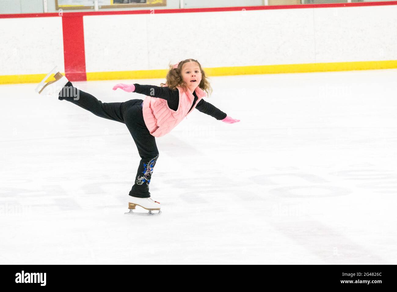 Little girl practicing figure skating moves on the indoor ice rink ...