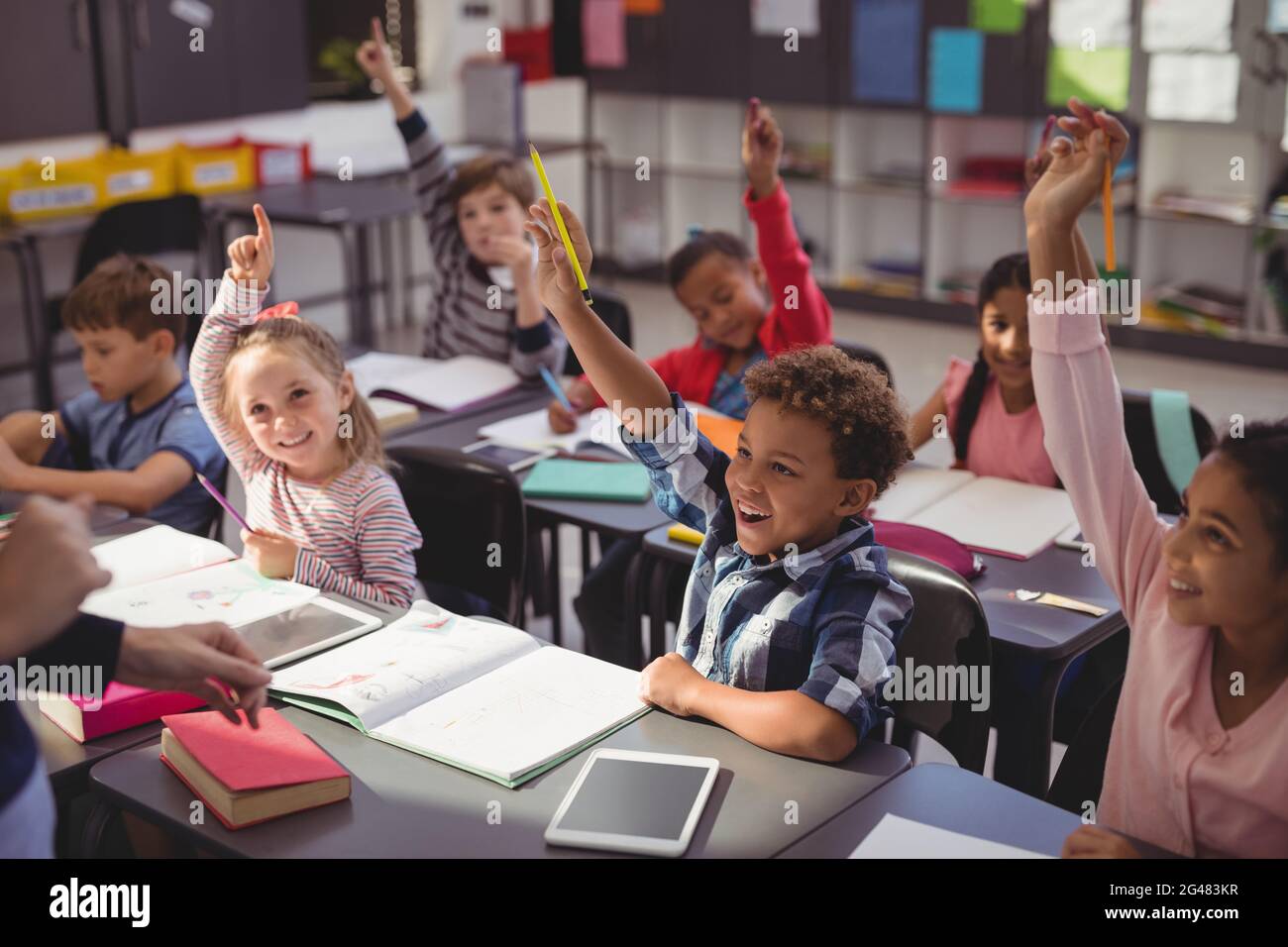 Schoolkids raising their hands in classroom Stock Photo - Alamy