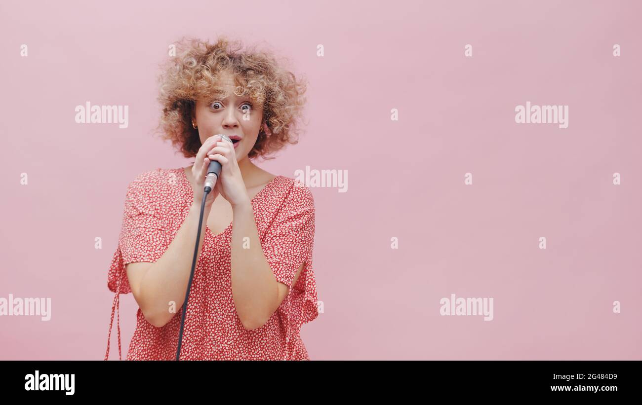 Cute girl singing with a microphone in her hand. Girl looking surprised ...